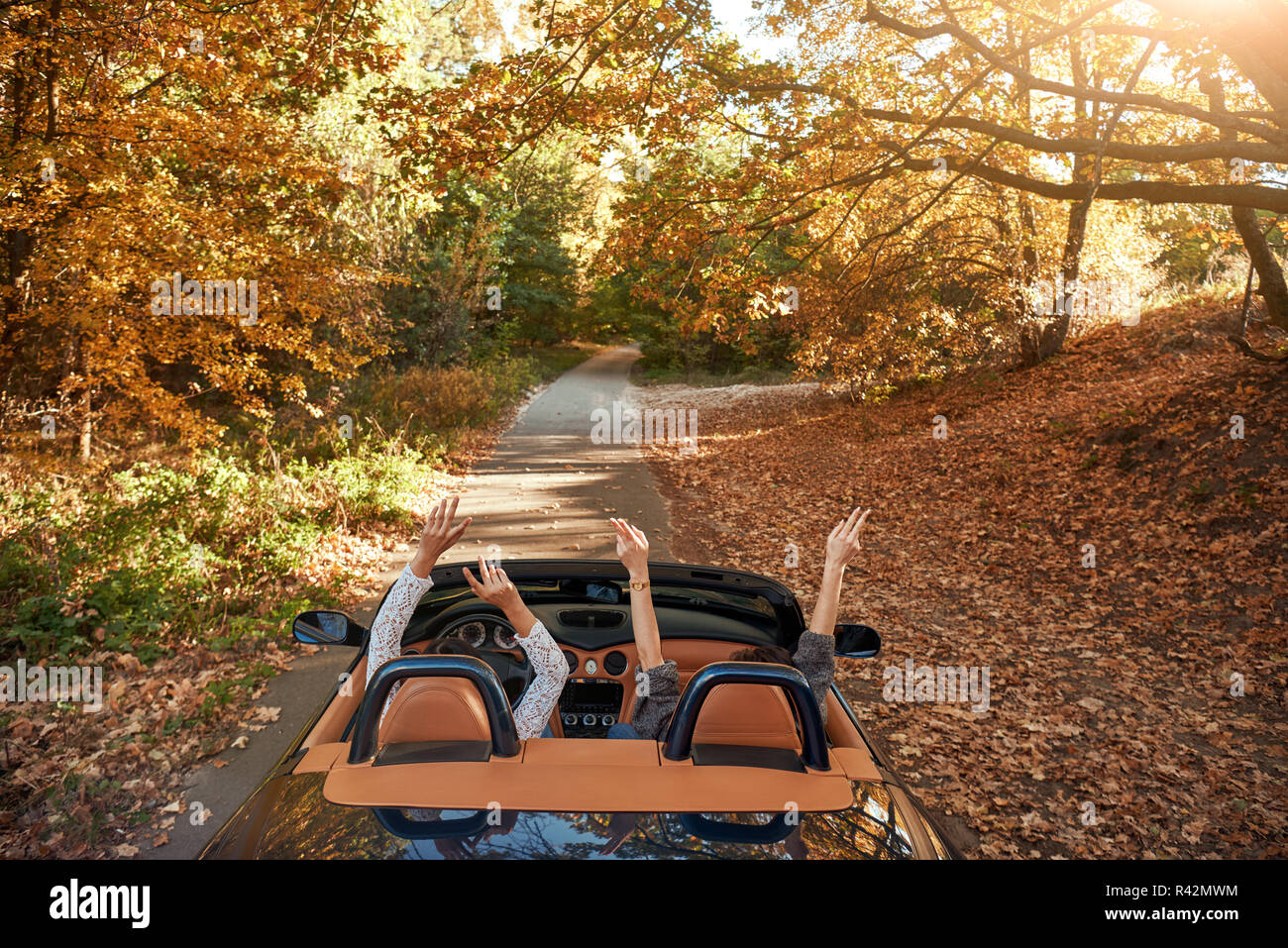 Female friends driving cabriolet with the hands up and having fun on ...