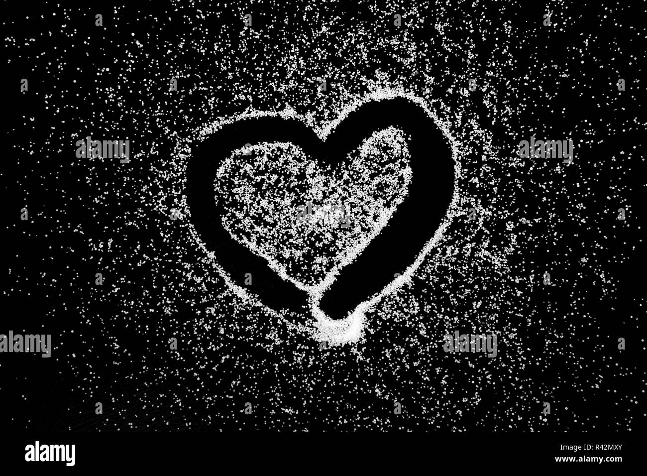 Love heart symbol drawing by finger on white salt powder on black ...