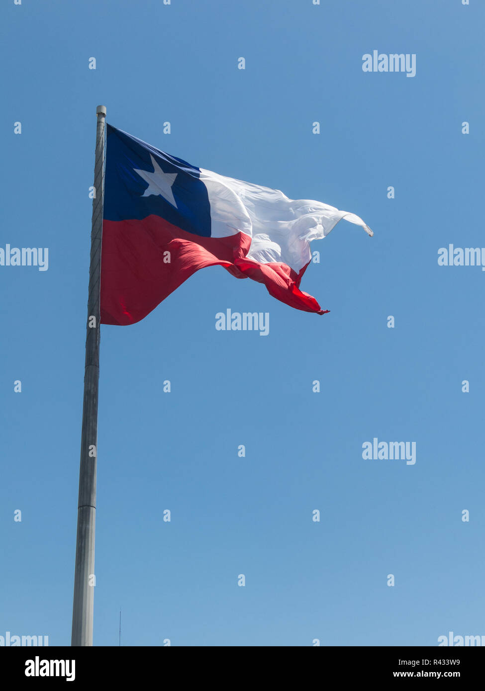 Flag of Chile flies in a strong wind against a bright blue sky with sun ...