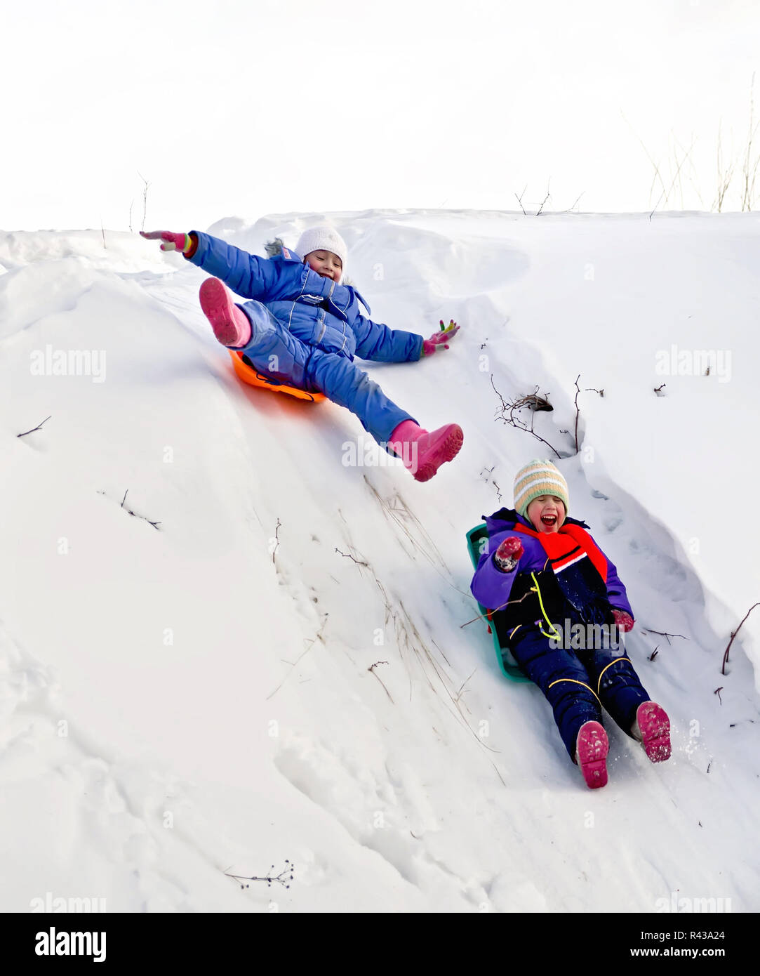Two girls on sled through the snow to slide Stock Photo - Alamy