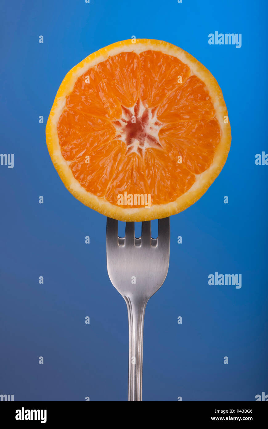 Orange fruit half fork blue background concept Stock Photo - Alamy