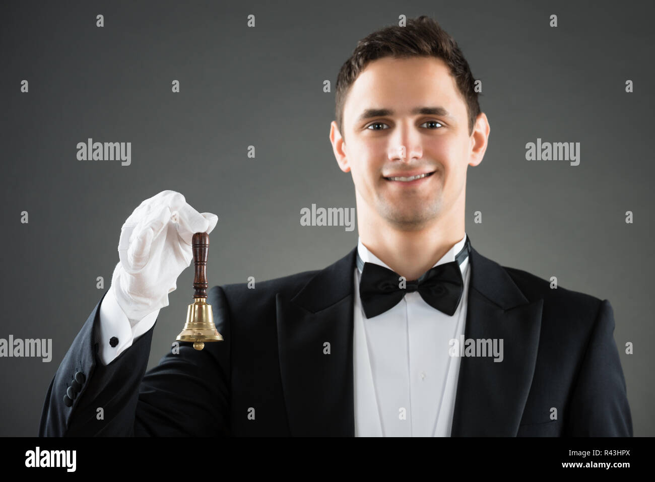 Portrait Of Smiling Waiter Holding Ring Bell Stock Photo - Alamy