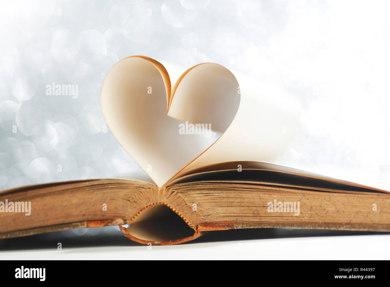 Pages of open book rolled in heart shape on glitter background Stock ...