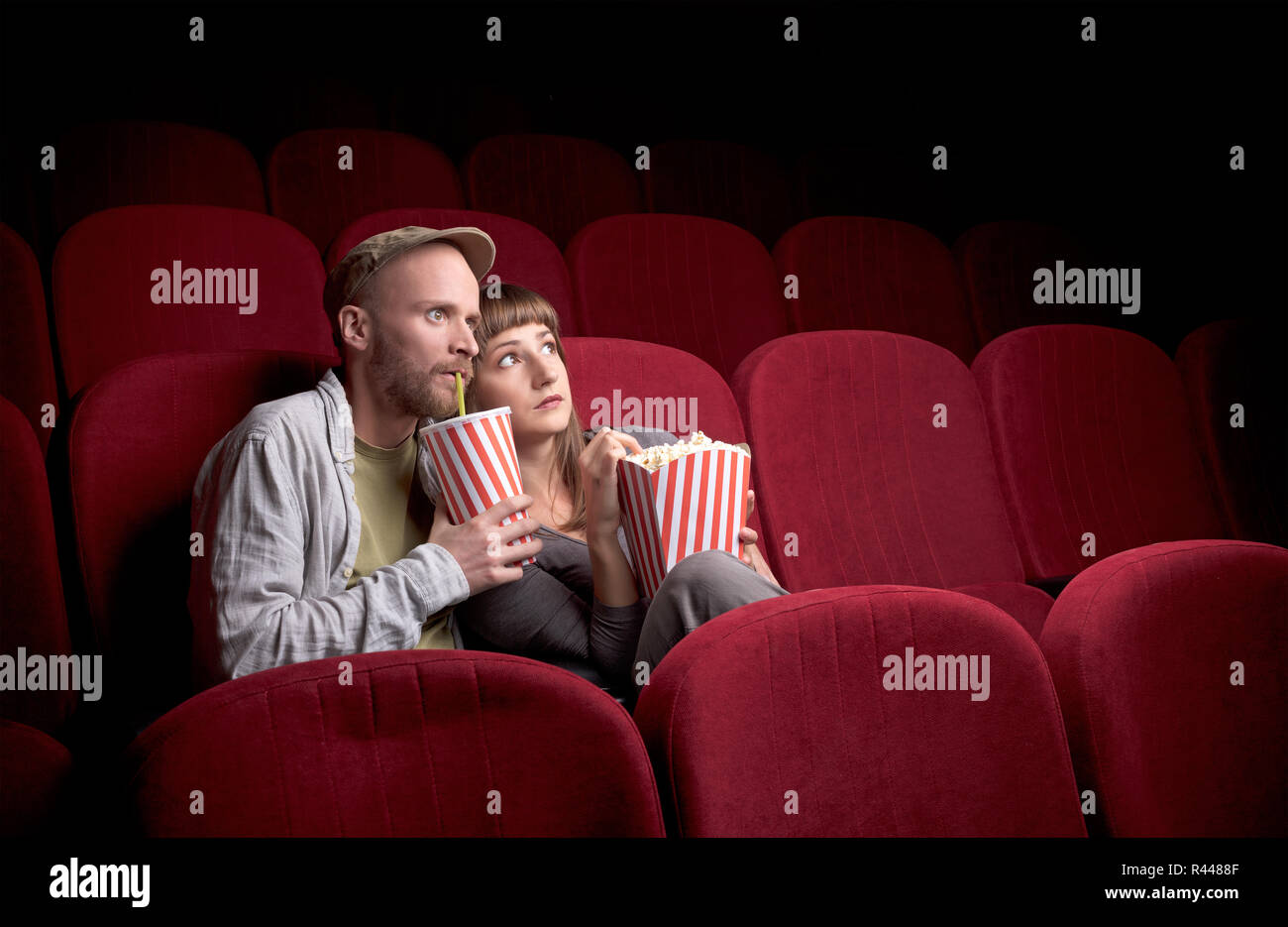 Young cute couple sitting alone at red movie theatre and having fun ...