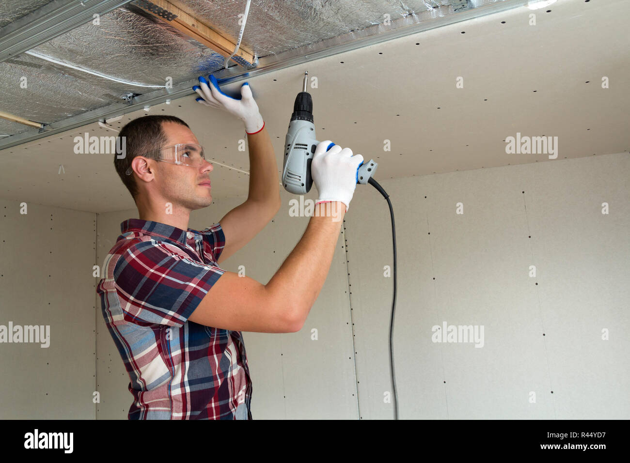 Young man in goggles fixing drywall suspended ceiling to metal frame ...