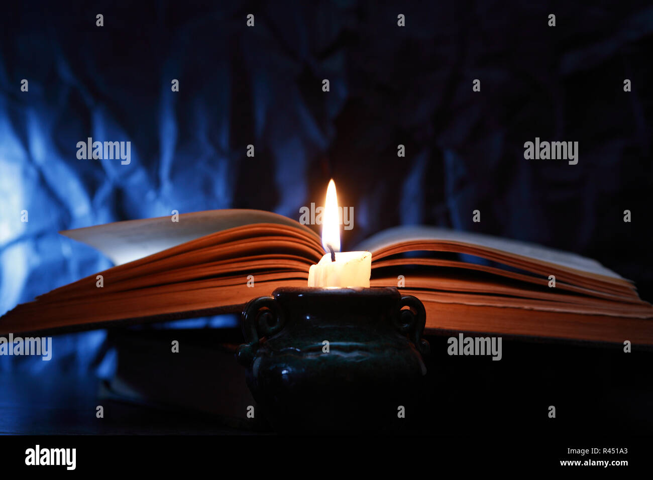 Still life with lighting candle near old book on dark blue background ...