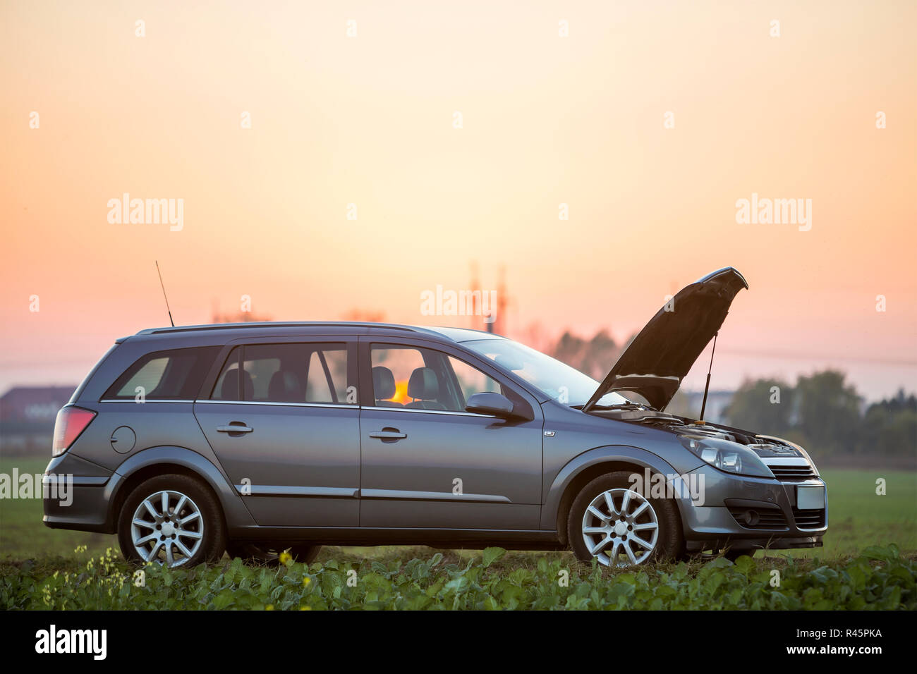 Side view of empty silver car with open hood on empty gravel field road ...
