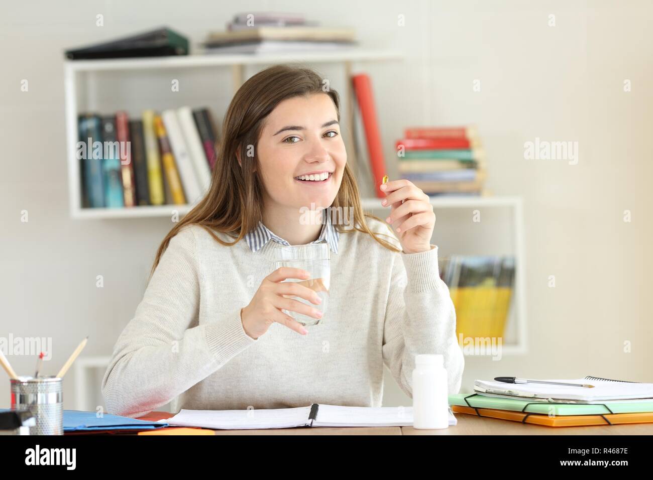 Happy student holding a vitamin pill supplement in a desk at home Stock ...