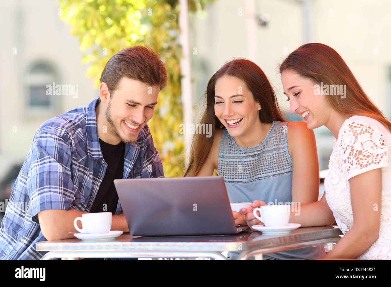 Three happy friends watching on-line media content on laptop in a bar ...