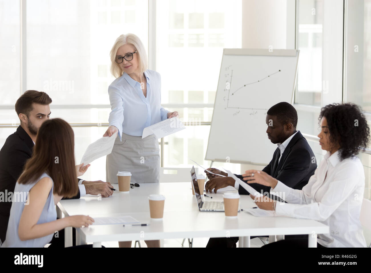 Smiling mature manager giving handouts to diverse employees at m Stock ...