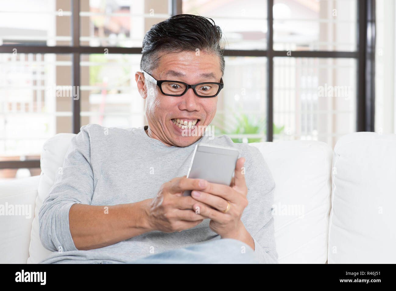Mature Asian man getting excited while using smartphone Stock Photo - Alamy