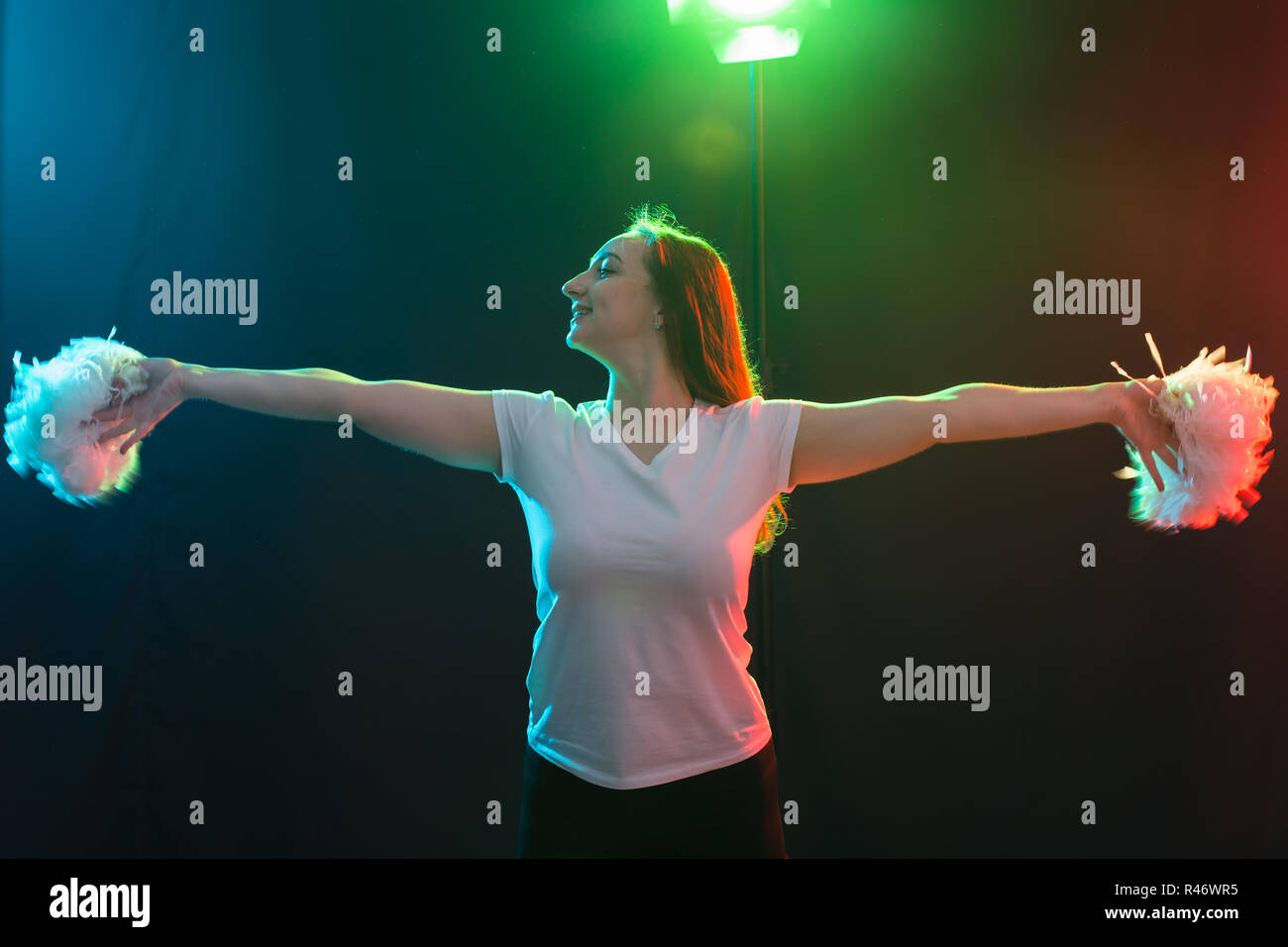 Cheerleading young woman dancing with pom-poms on colourful background ...