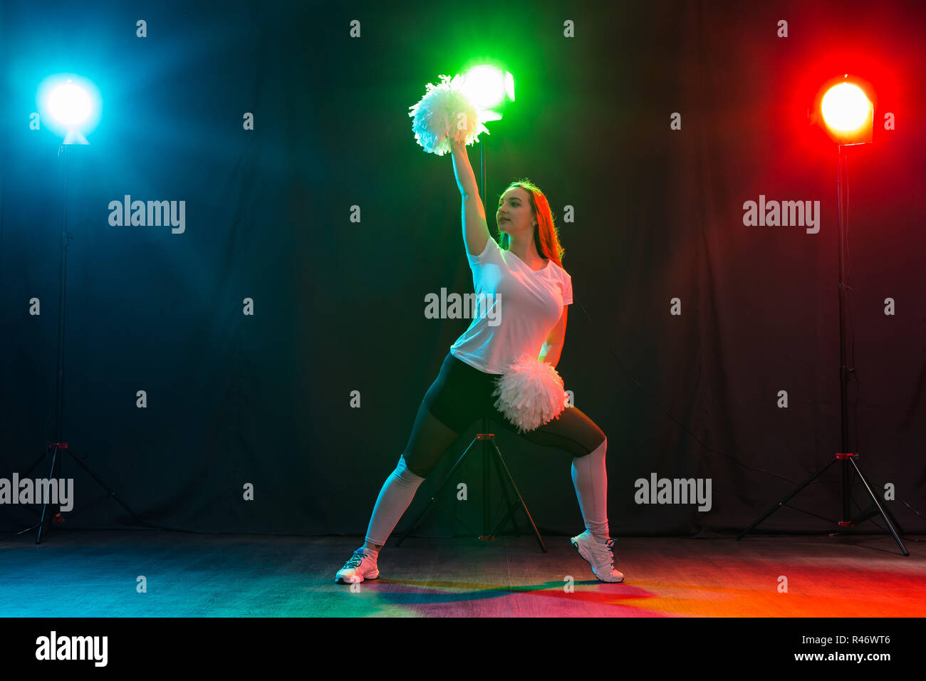 Cheerleading young woman dancing with pom-poms on colourful background ...