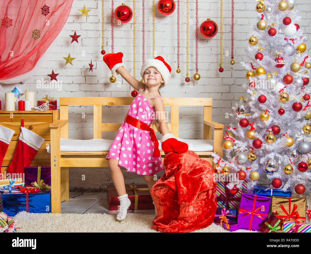 Girl in a cap and mittens of Santa Claus dancing around the bag with ...