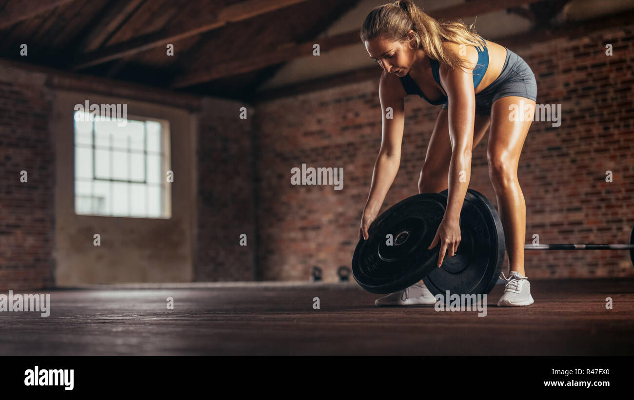 fitness woman adding weights to the barbell. Athlete preparing weights ...