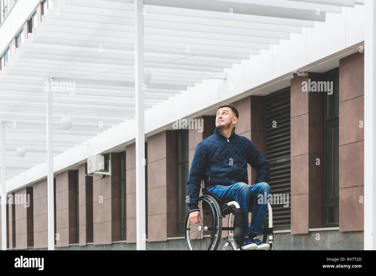 Young man in a wheelchair against the backdrop of a modern high-rise ...
