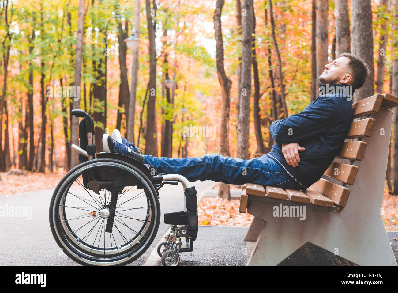Young man resting sitting on a bench with his legs on his wheelchair ...