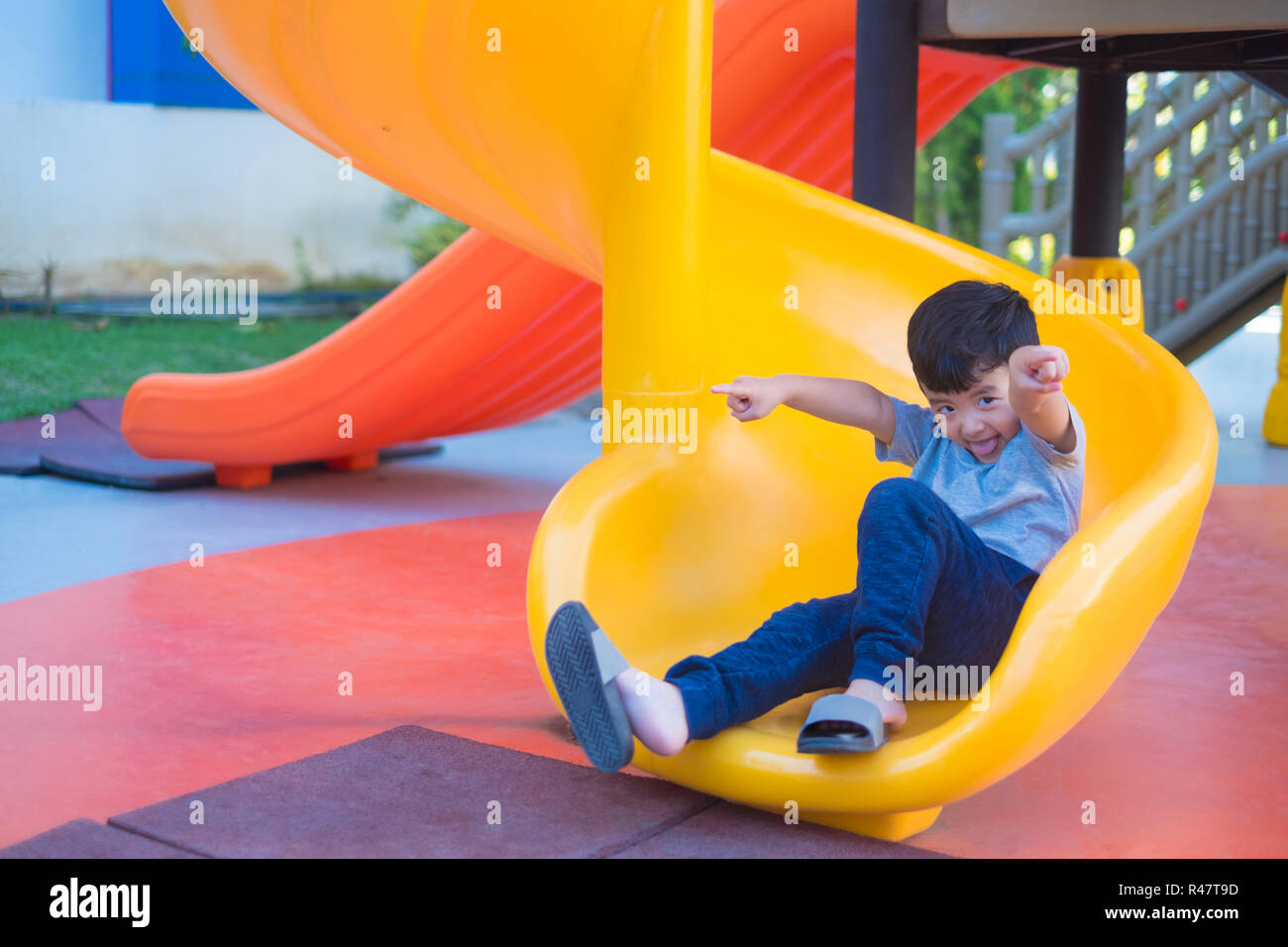 Asian kid playing slide at the playground under the sunlight in summer ...