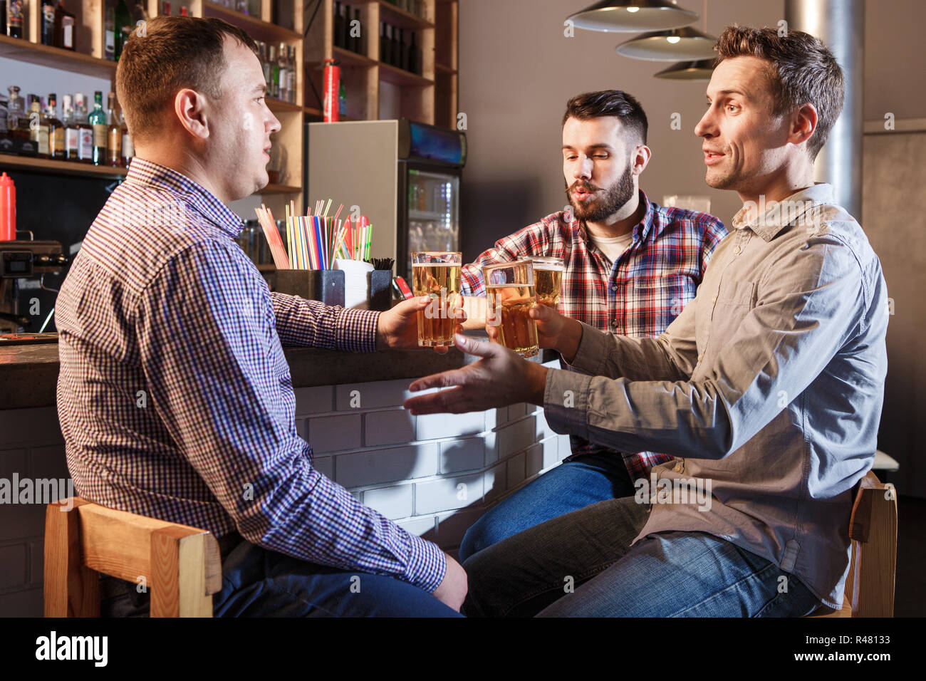 Happy friends drinking beer at counter in pub Stock Photo - Alamy