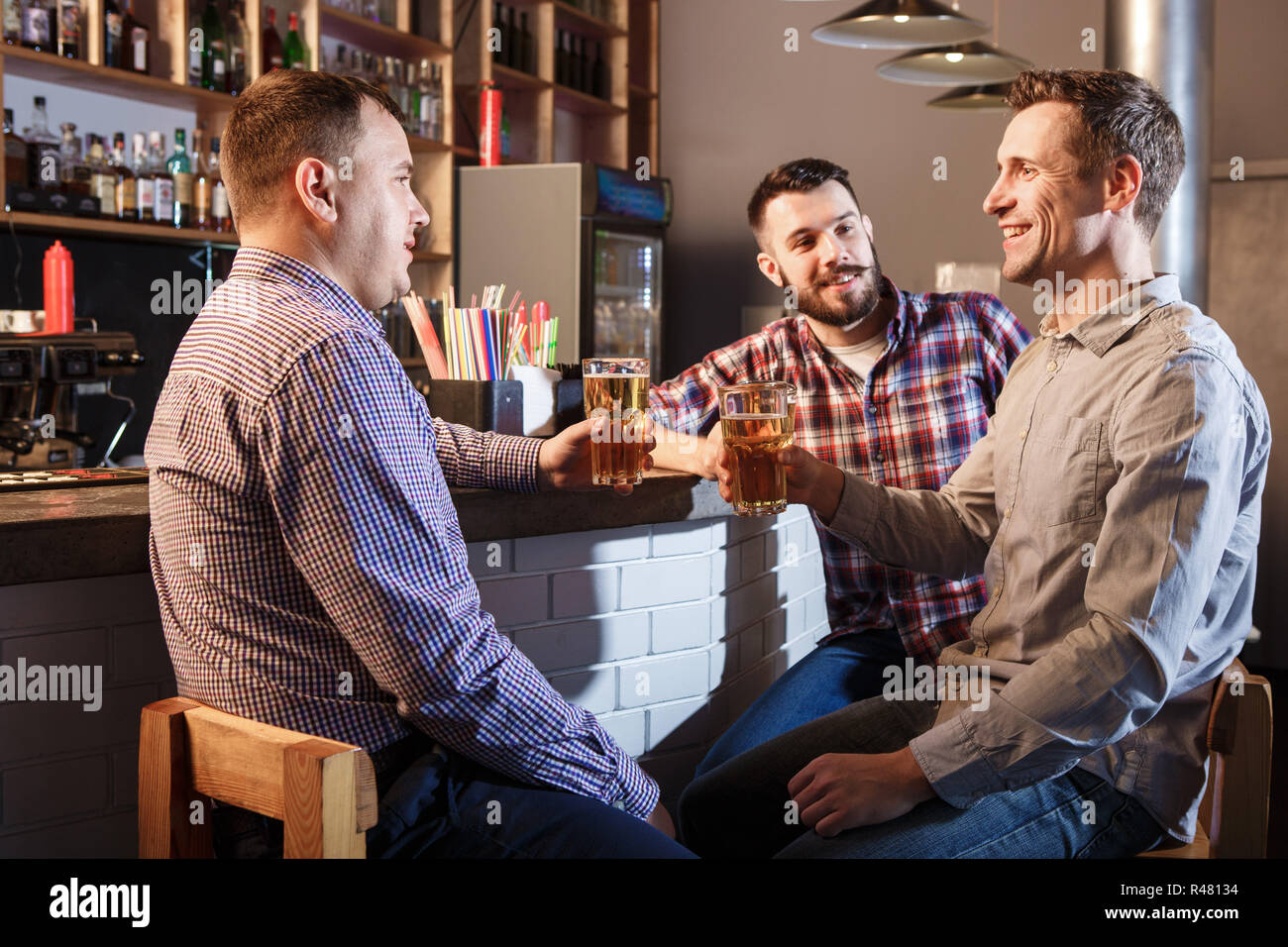 Happy friends drinking beer at counter in pub Stock Photo - Alamy
