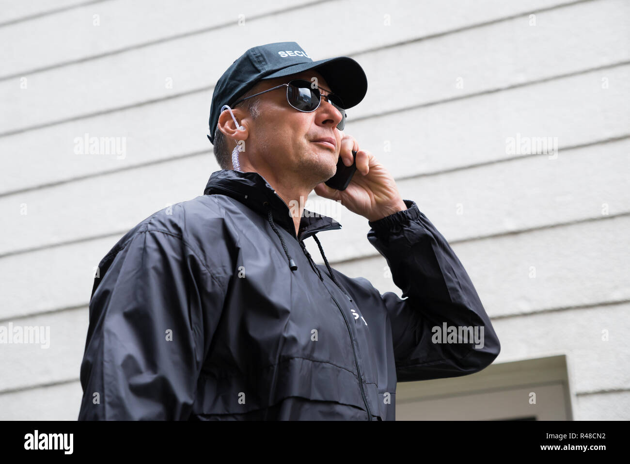 Confident Security Guard Listening To Earpiece Against Building Stock ...