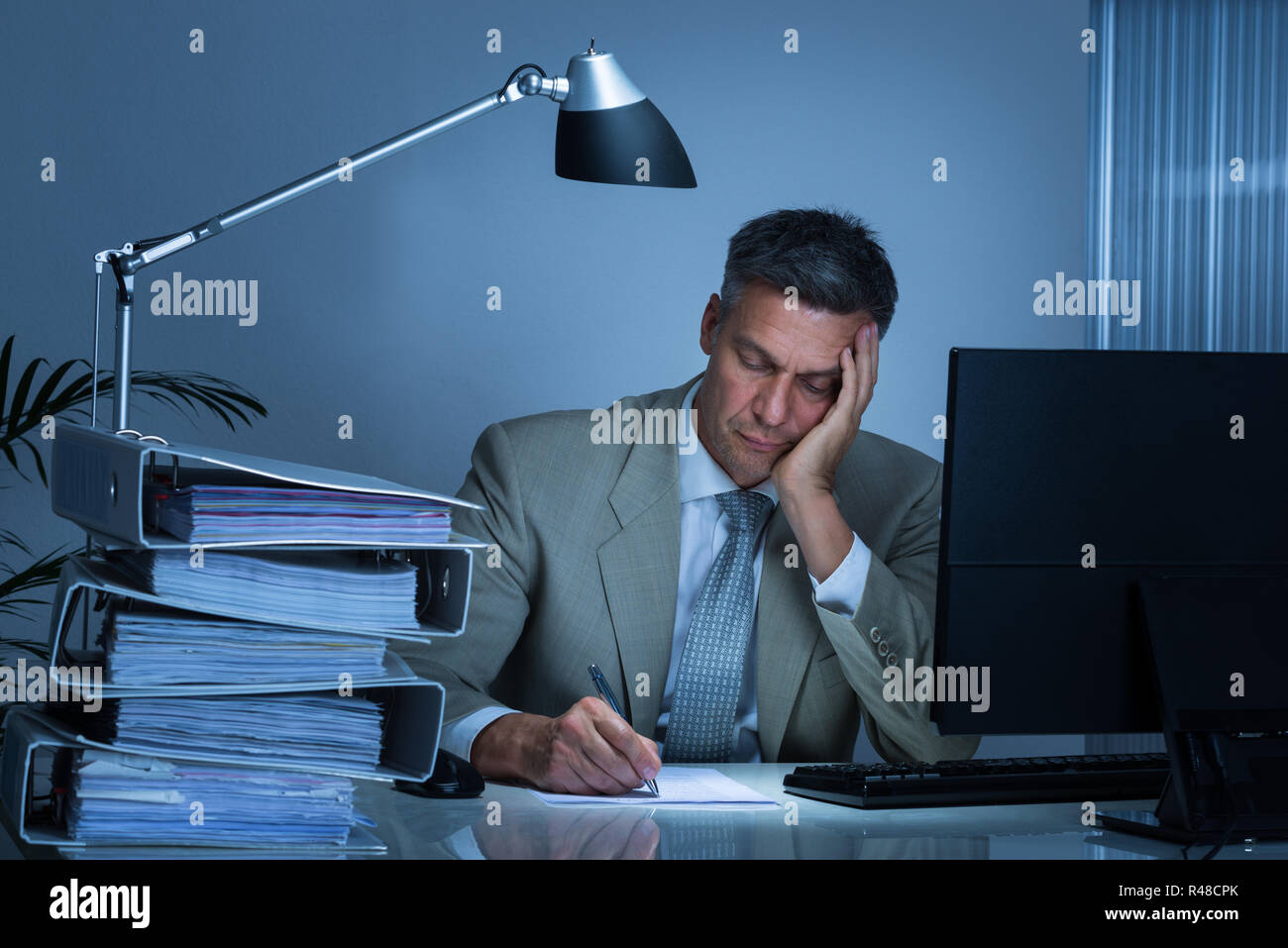 Tired Businessman Writing On Document While Working Late Stock Photo ...