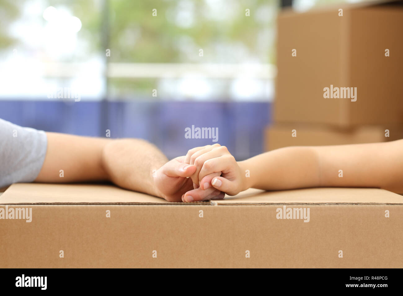 Couple holding hands over a box moving home Stock Photo - Alamy