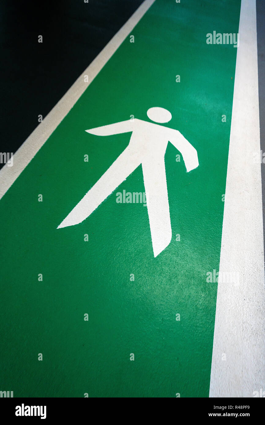white walking man symbol on green tarmac walkway in an airport carpark ...