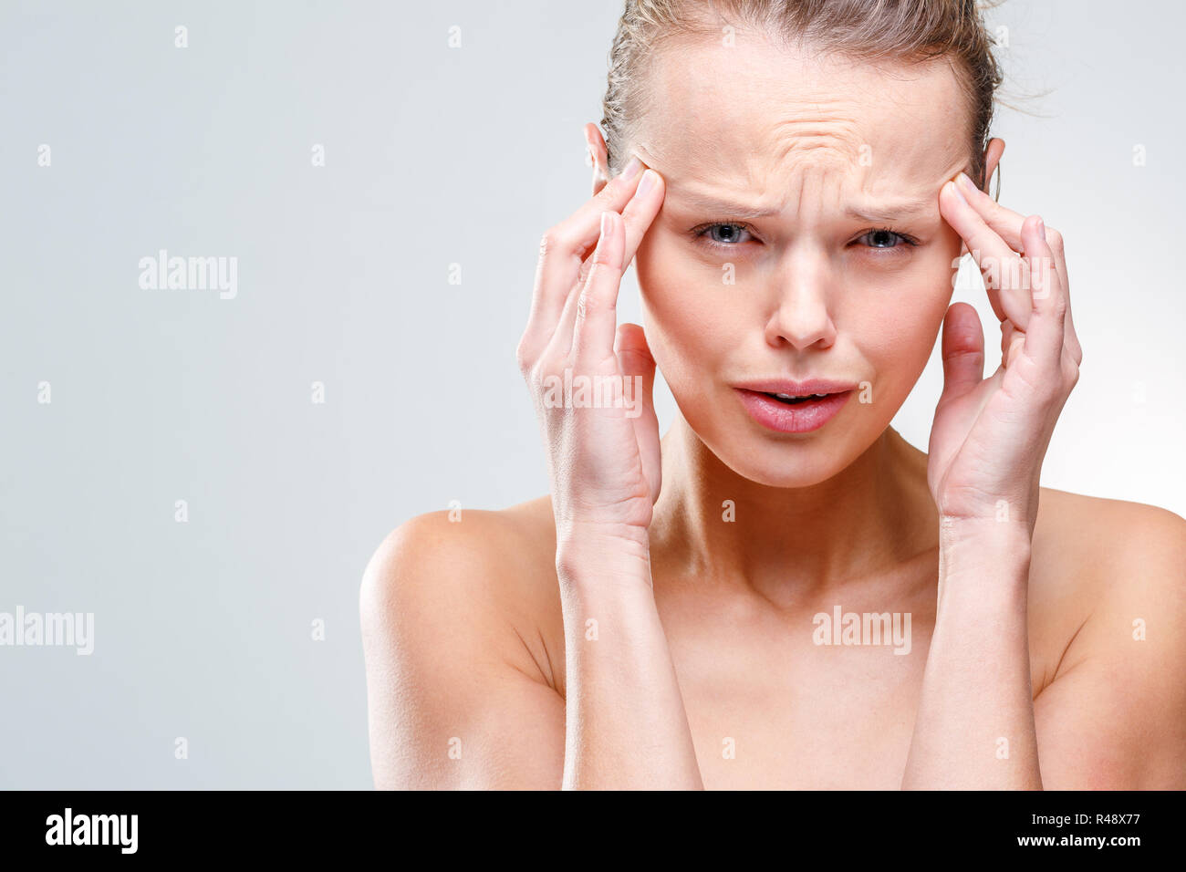 Beautiful woman suffering from acute headache over grey clean ...