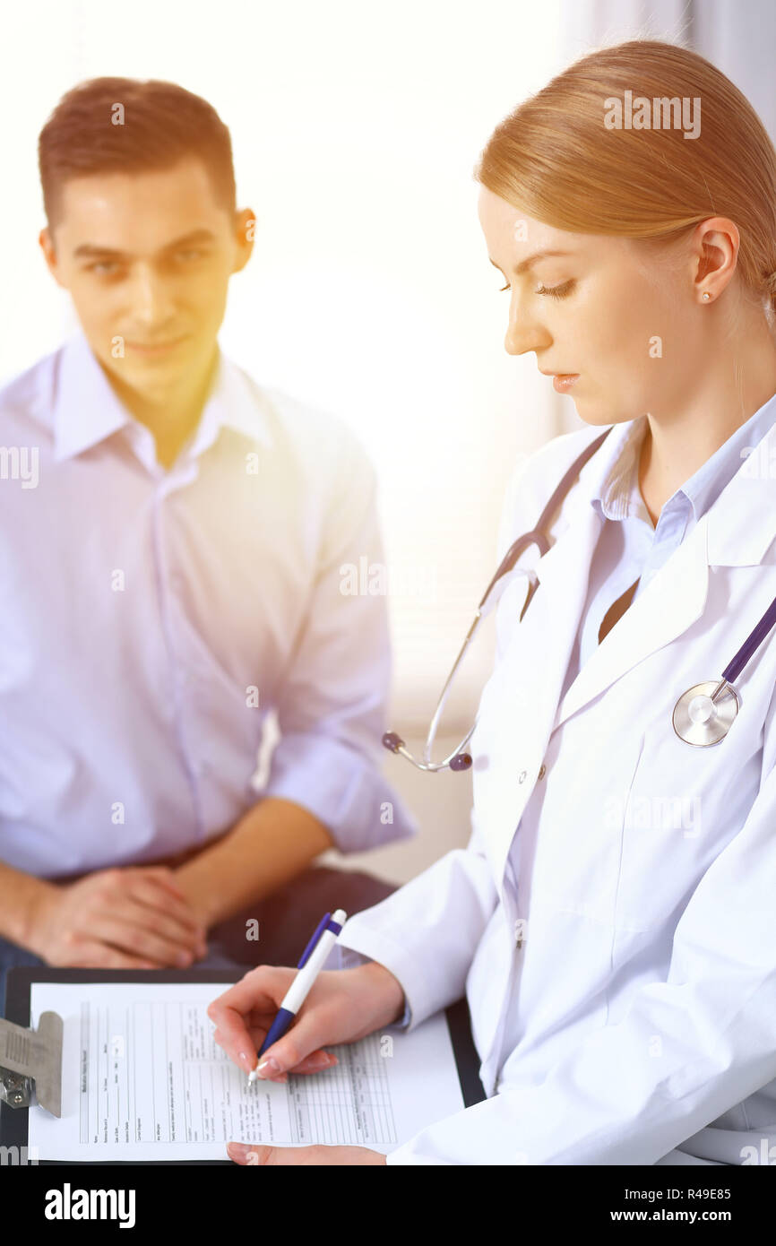 Female doctor holding application form while consulting man patient in ...