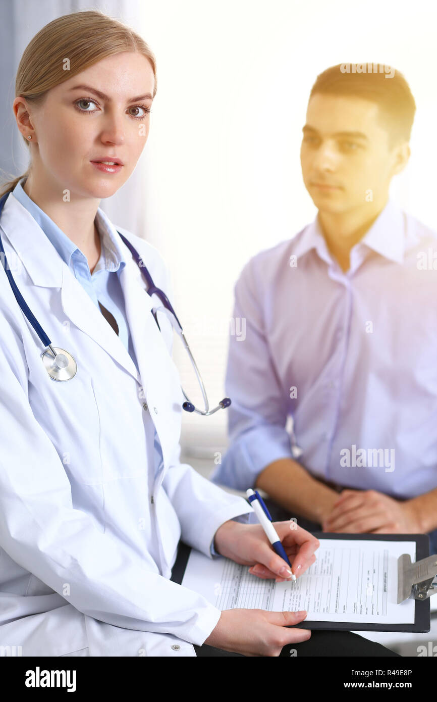 Female doctor holding application form while consulting man patient in ...