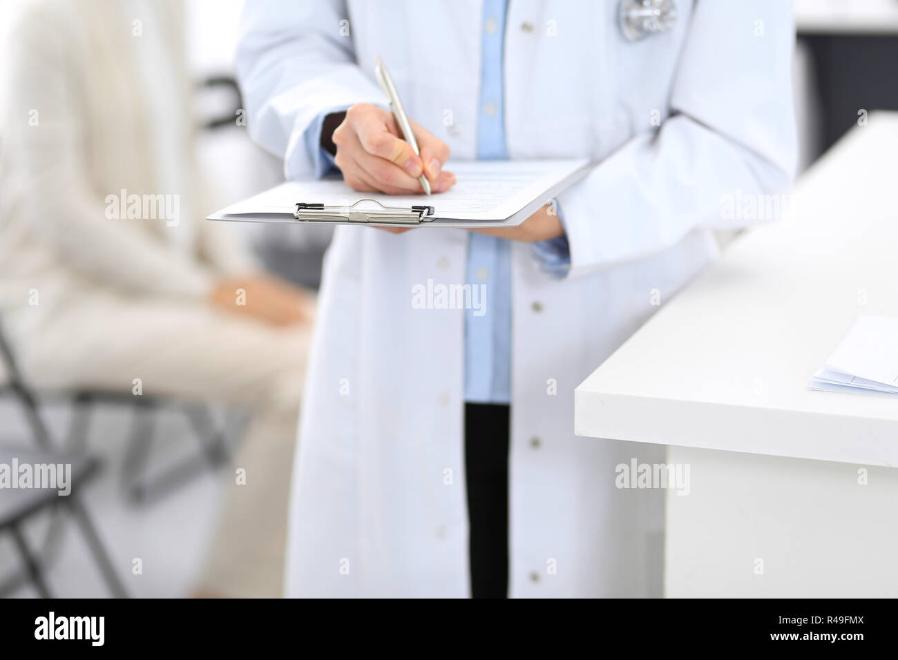 Doctor woman filling up medical form while standing near reception desk ...