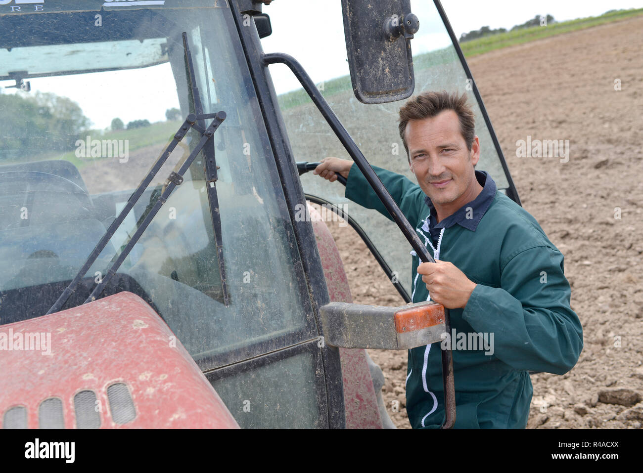 Farmer climbing into tractor out in farming land Stock Photo - Alamy