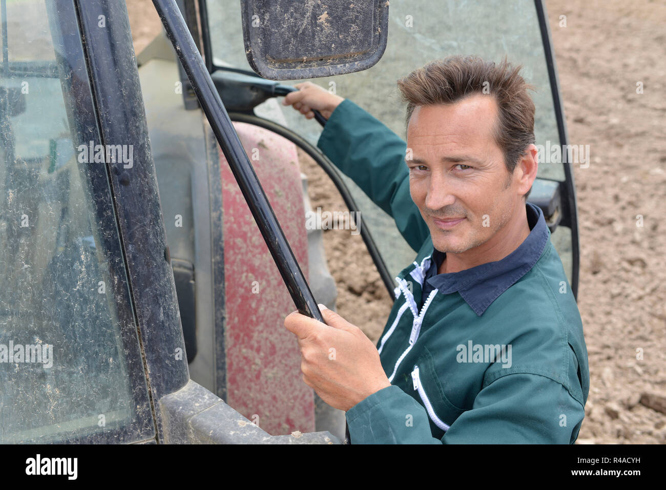 Farmer climbing into tractor out in farming land Stock Photo - Alamy