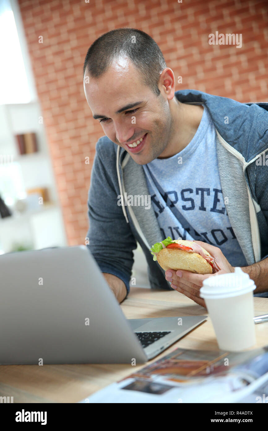 Student eating sandwich in front of laptop Stock Photo - Alamy