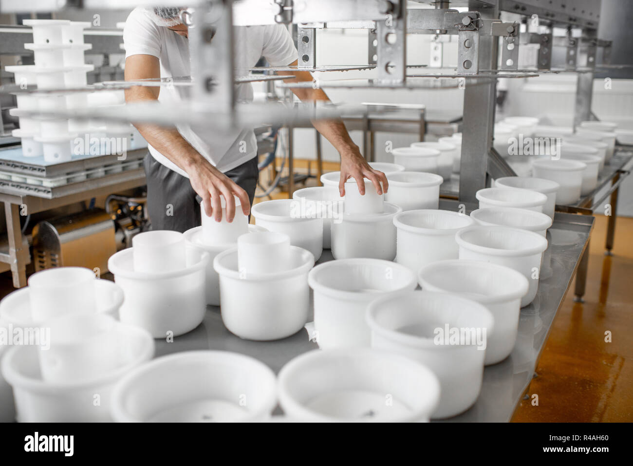 Man in uniform forming cheese into the plastic molds putting them under ...