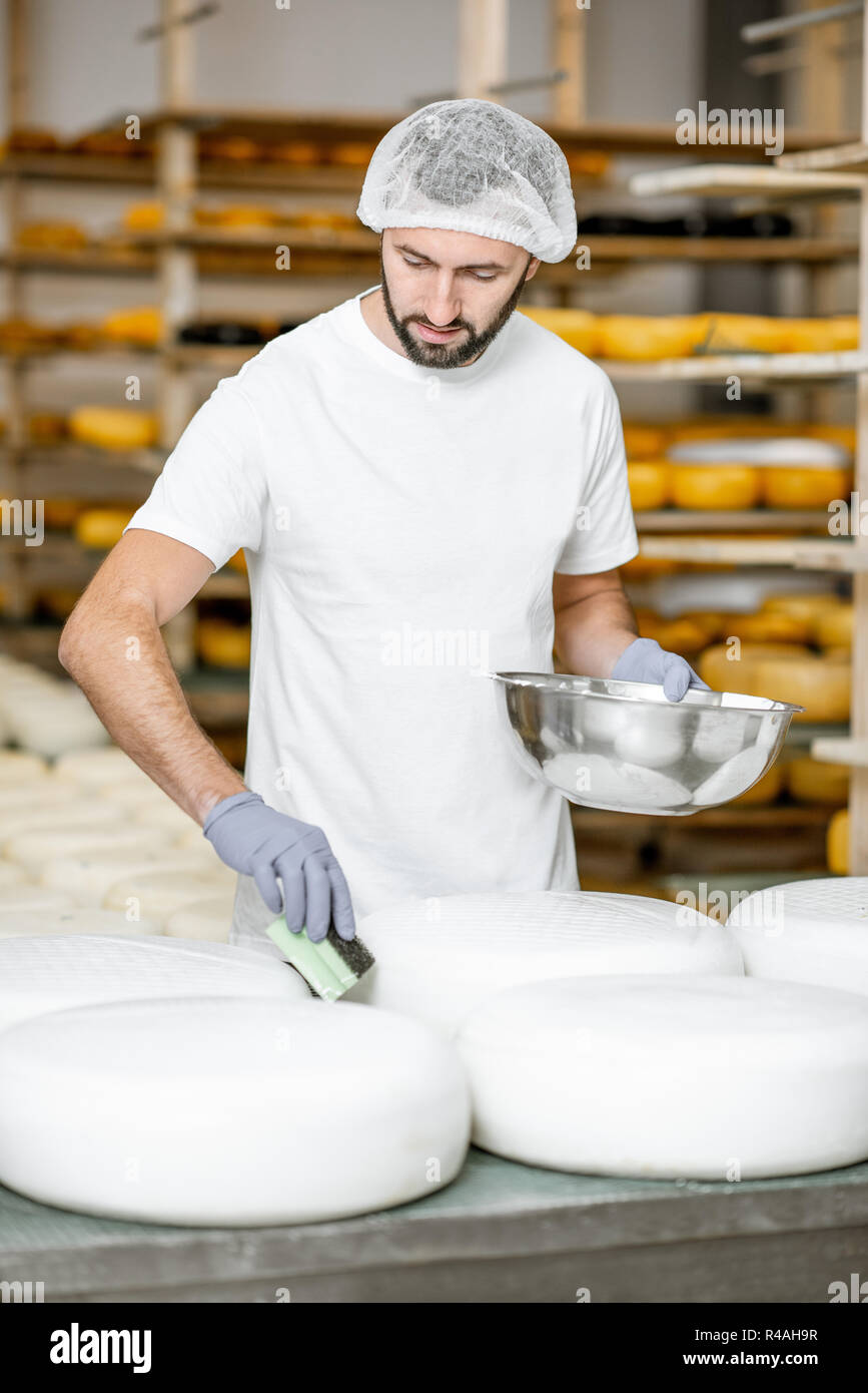 Man rubing cheese wheels with wax at the cheese manufacturing with ...