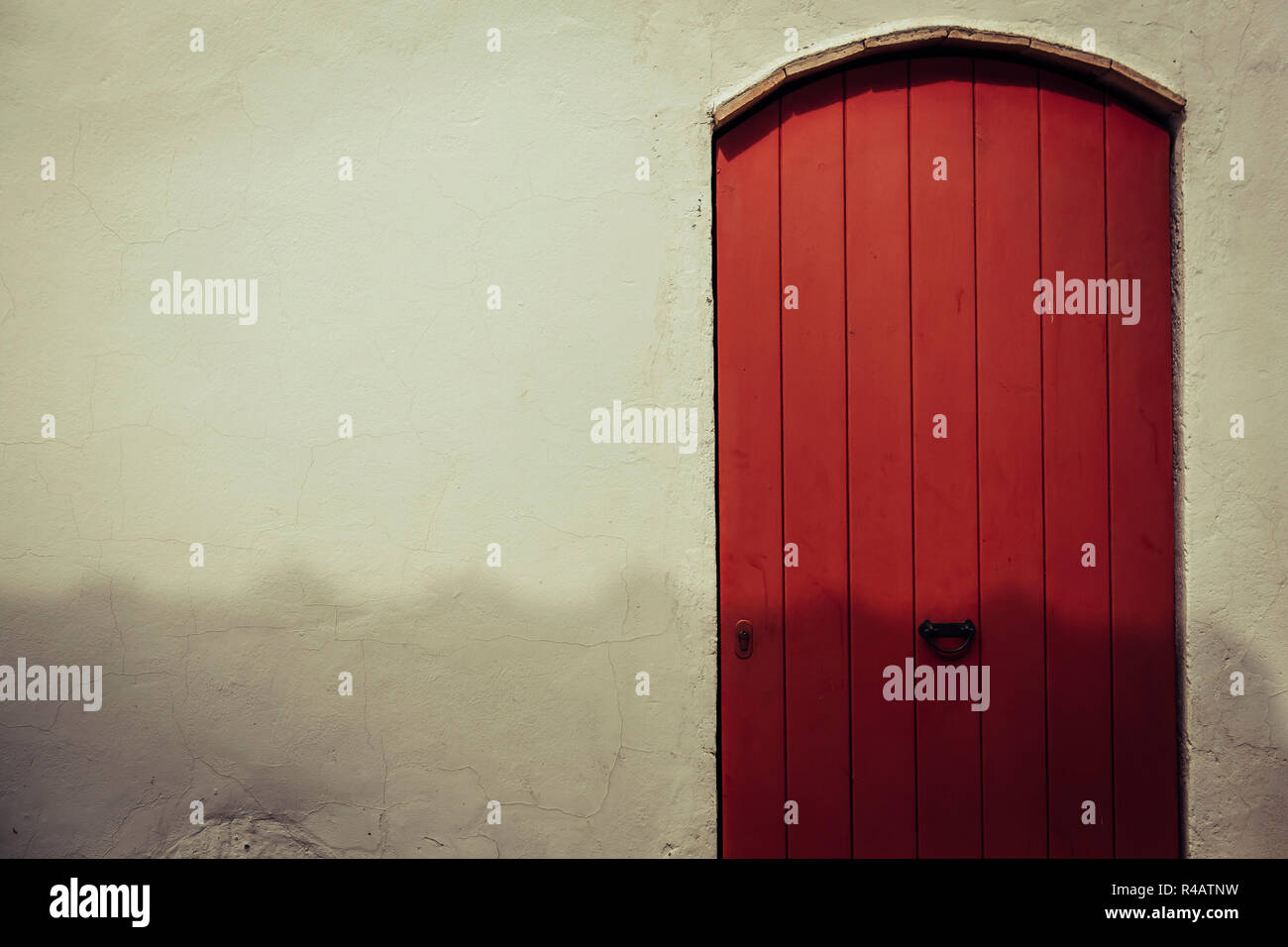 Large red painted wooden door set in to a plain white wall in the warm ...