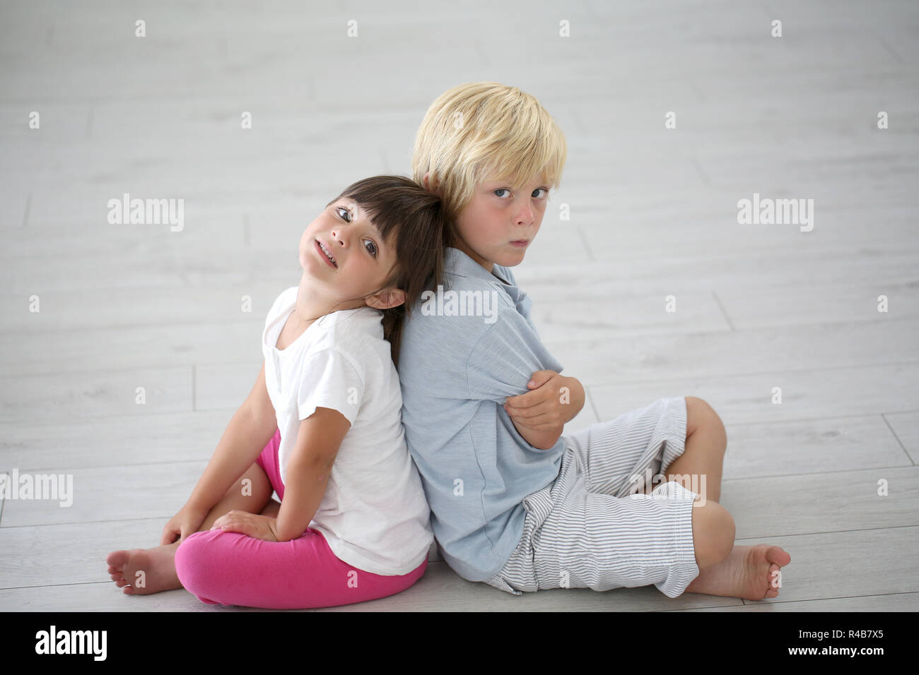 Brother and sister sitting back to back on the floor Stock Photo - Alamy