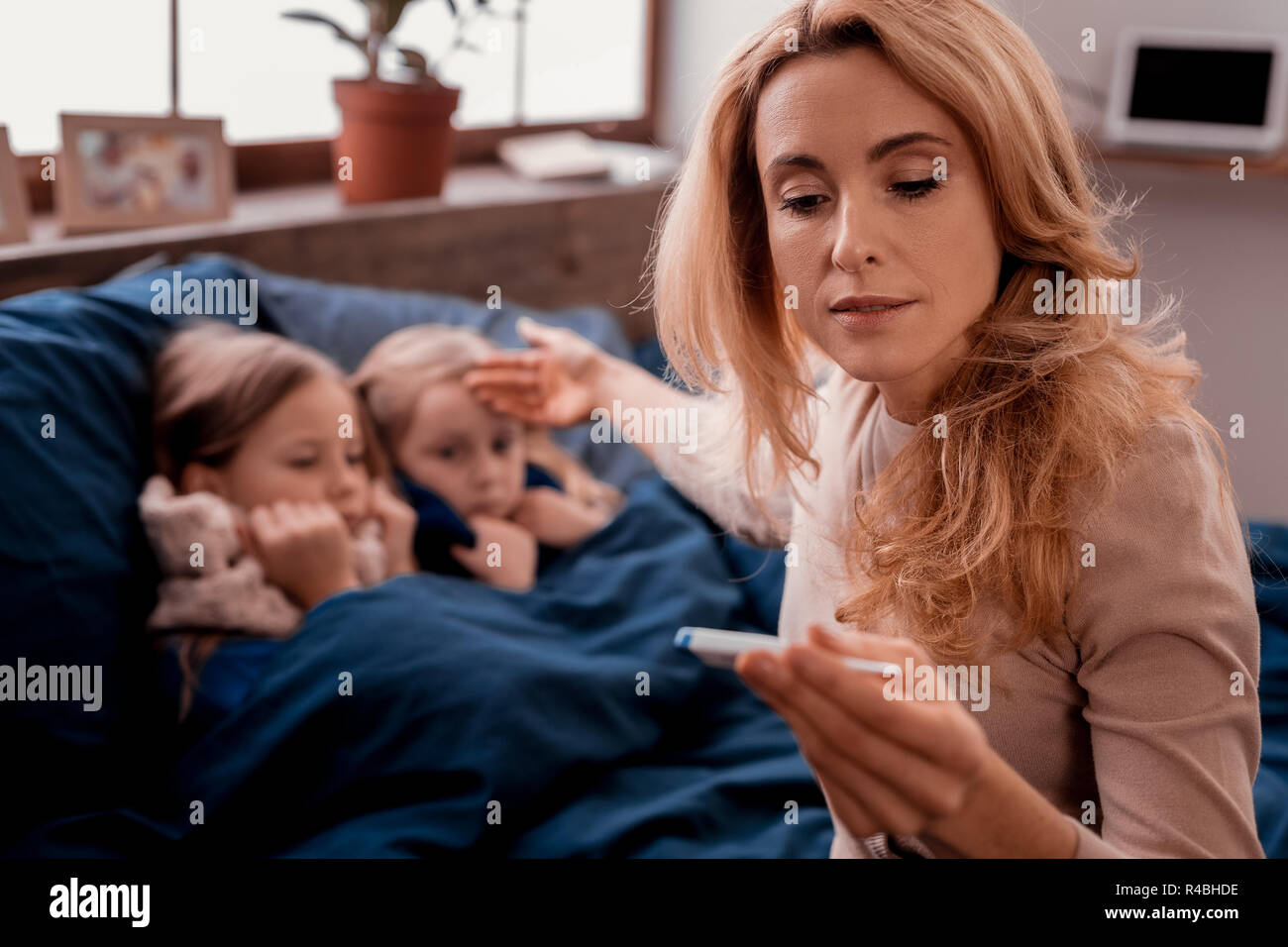 Fever. Anxious serious lady worrying while taking daughters temperature ...