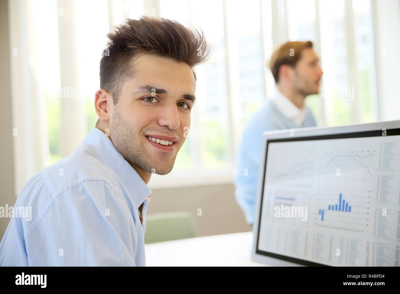 Office worker sitting in front of desktop, colleagues in background ...