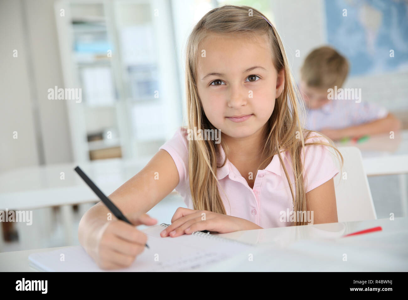 Cute schoolgirl writing on notebook, in classroom Stock Photo - Alamy