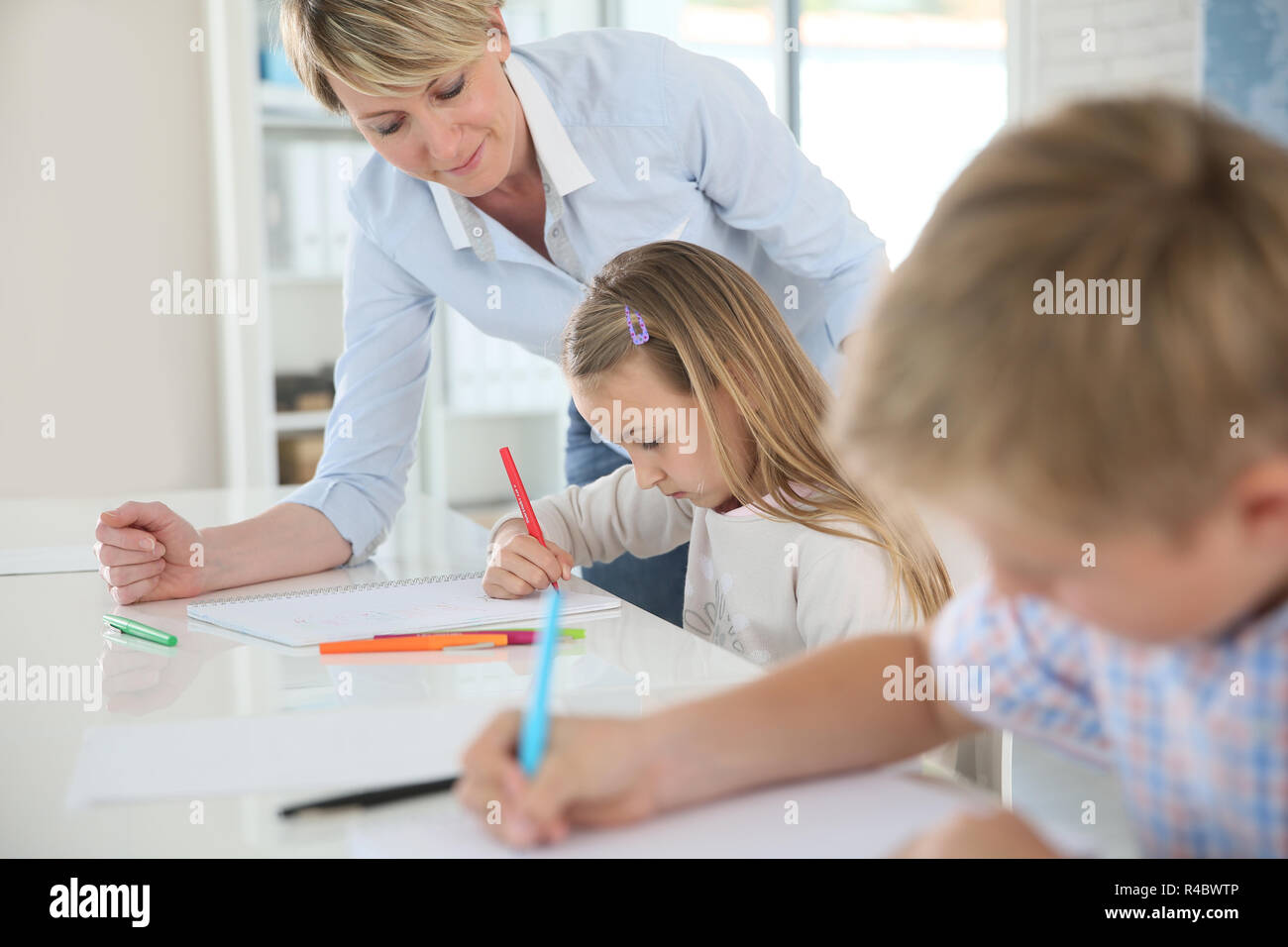 Teacher helping kids in classroom Stock Photo - Alamy