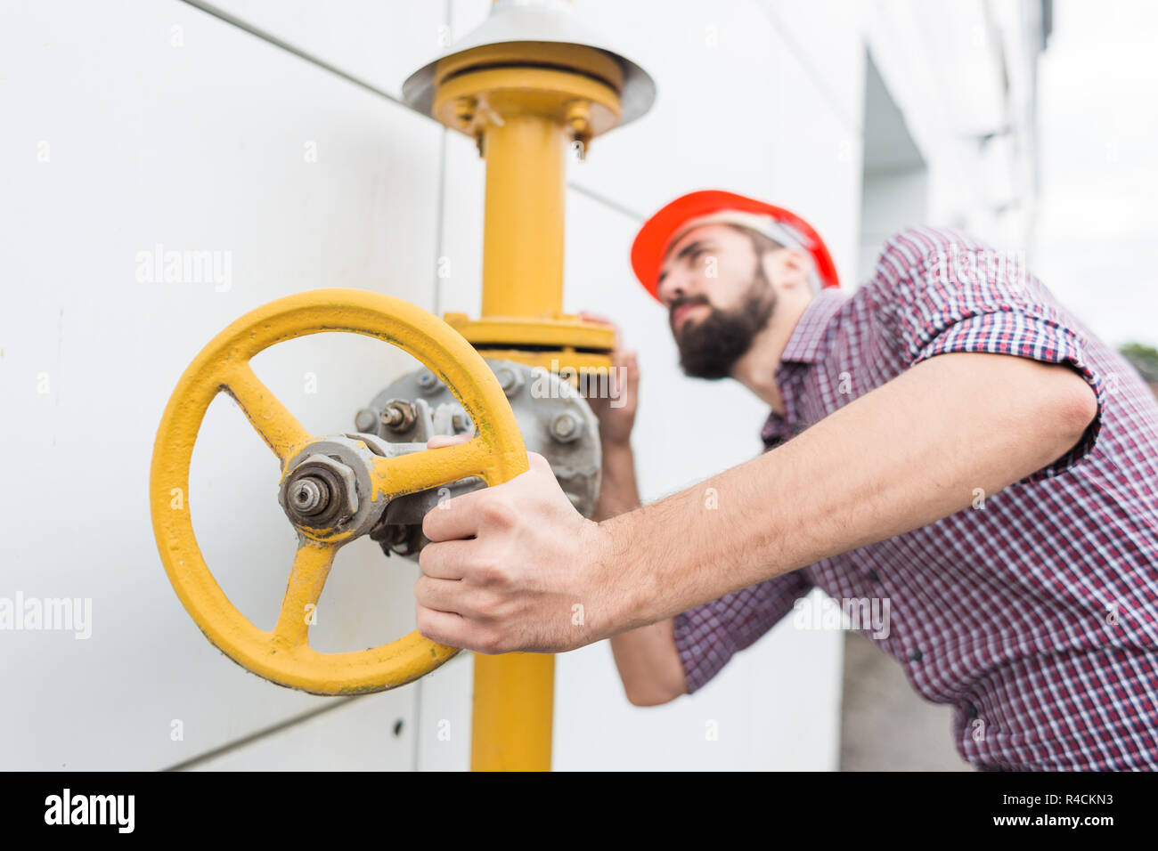 power station worker. man engineer in helmet and shirt twist gas pipe ...
