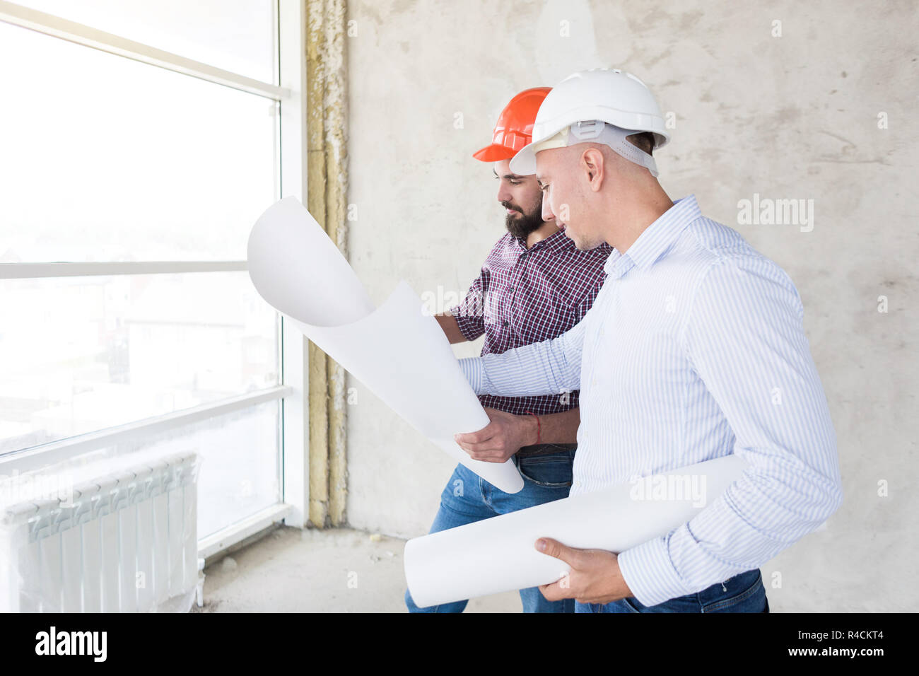 male engineers, architects in helmets stand by the window and hold a ...