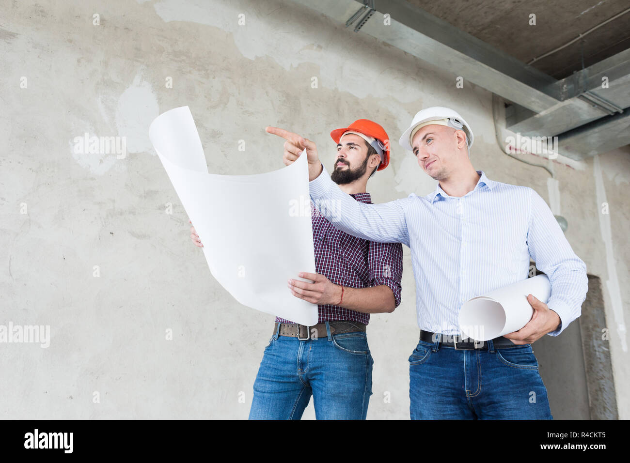 male engineers, architects in helmets stand by the window and hold a ...