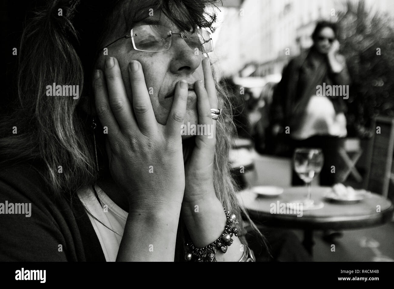 woman, eyes shut, head in hands dreaming, sitting at outside cafe table ...