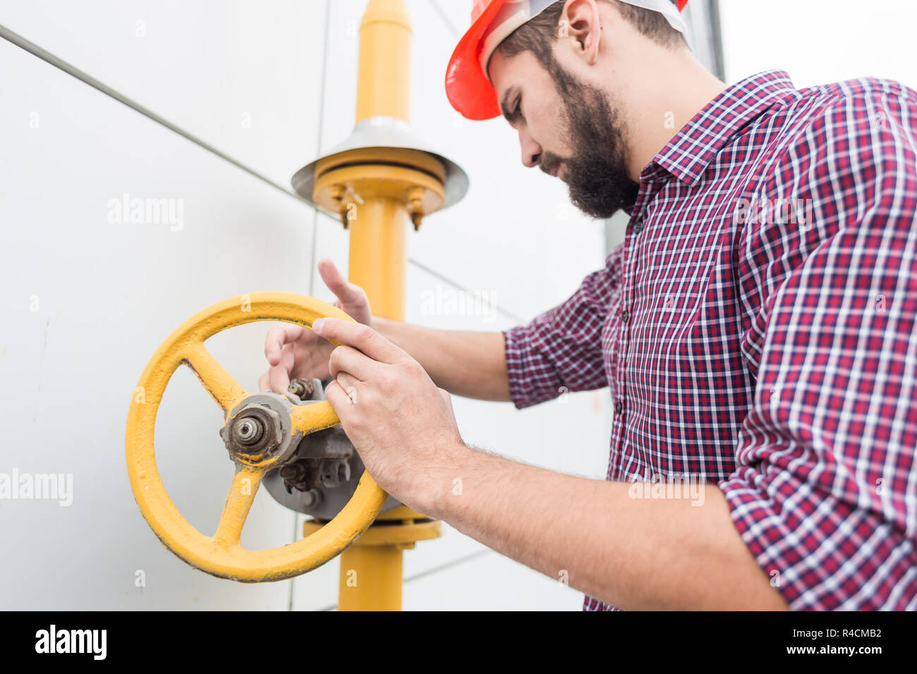 power station worker. man engineer in helmet and shirt twist gas pipe ...