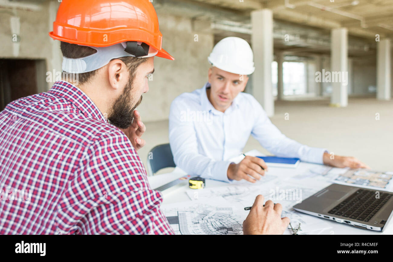 male engineers, architects working at the desk in helmets. Drawings ...