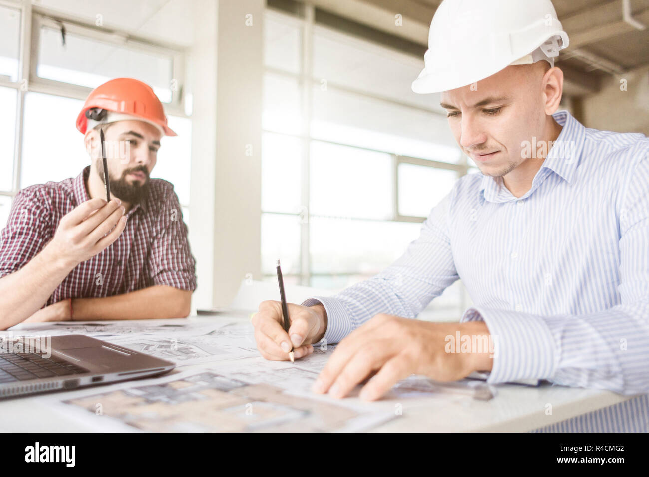 male engineers, architects working at the desk in helmets. Drawings ...